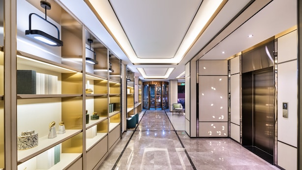Um corredor moderno com piso de mármore, prateleiras embutidas com objetos decorativos e área central com elevador.