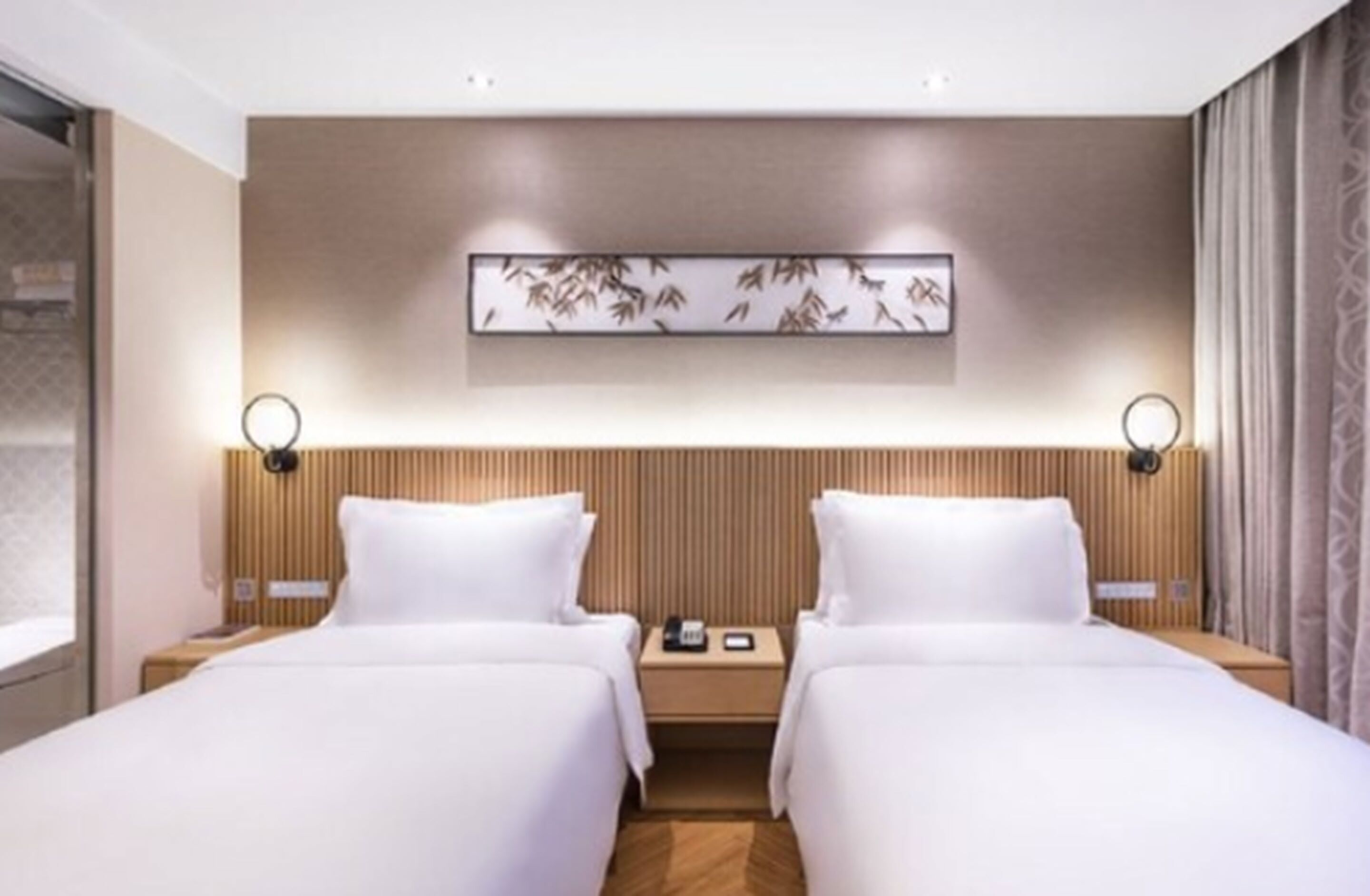 Quarto de hotel com duas camas, cabeceira de madeira, uma obra de arte na parede e luminárias de cabeceira.