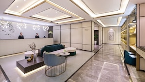 Um lobby moderno com balcão de recepção, área de estar e corredor que leva a uma escadaria.