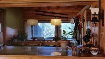 Um quarto tradicional japonês com vigas de madeira, piso de tatame e vista para o exterior. Há duas lanternas de papel penduradas no teto, um relógio e uma estátua na parede.