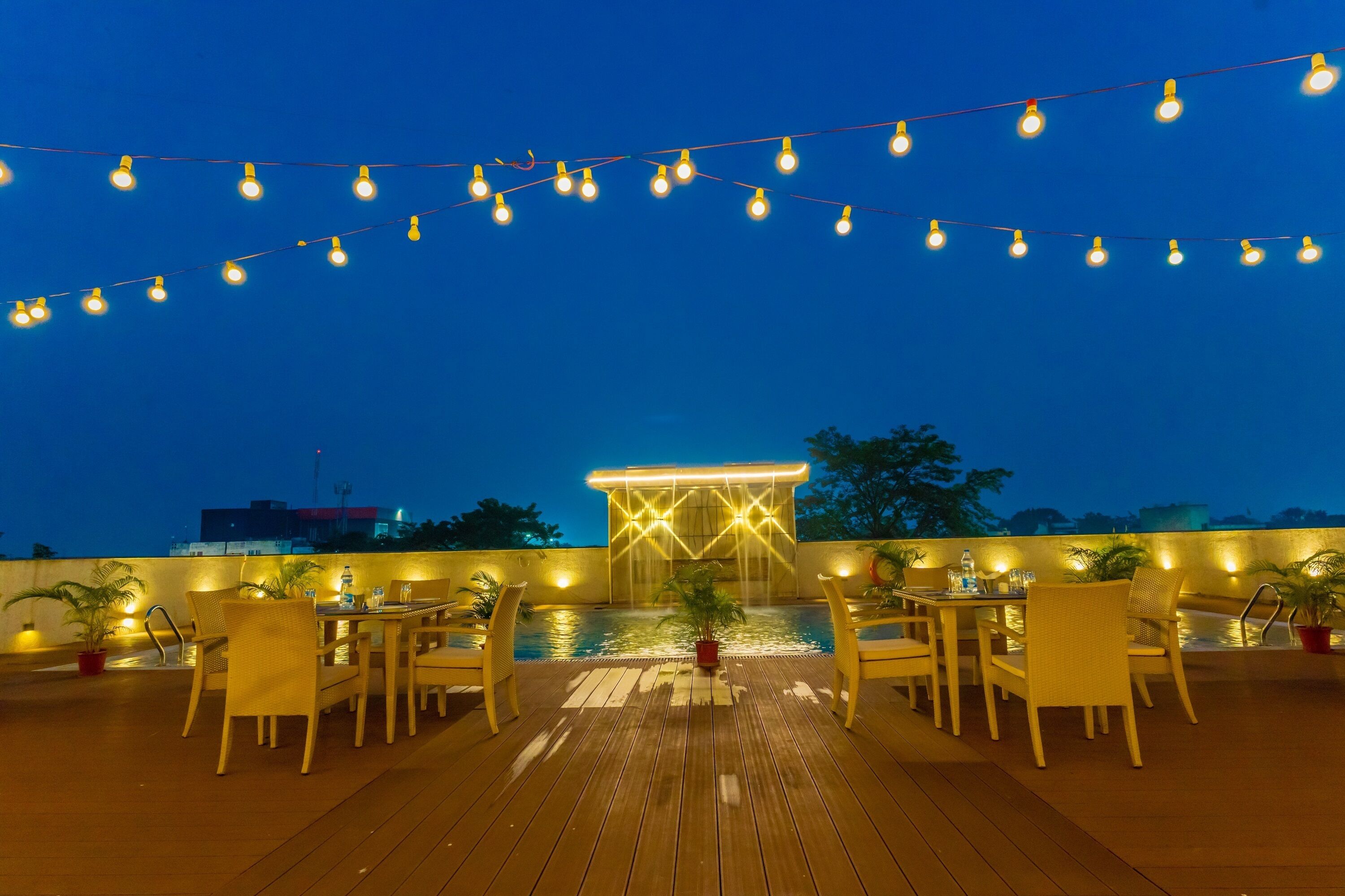 Uma área de refeições ao ar livre com luzes de Natal, piscina e uma cascata.