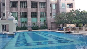 Piscina com deck revestido, rodeada por um edifício com várias janelas e entrada decorativa.