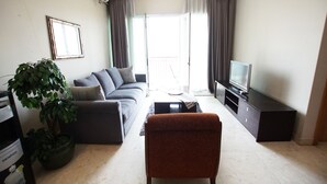 Uma sala de estar com sofá, televisão, mesa de centro e planta em vaso.