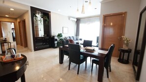 Uma sala de estar moderna com área de jantar, destacando uma mesa e cadeiras de madeira escura, um sofá e uma janela grande com cortinas.