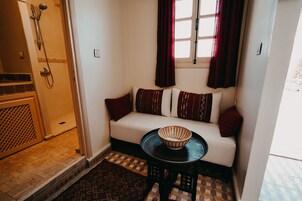 Quarto pequeno e acolhedor com sofá, uma mesinha com uma tigela, área de duche e chão estampado.