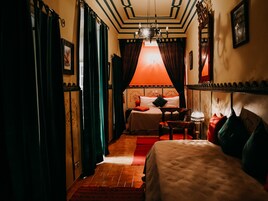 Quarto de hotel com cama, mesa de cabeceira, luminária e vista para o corredor.