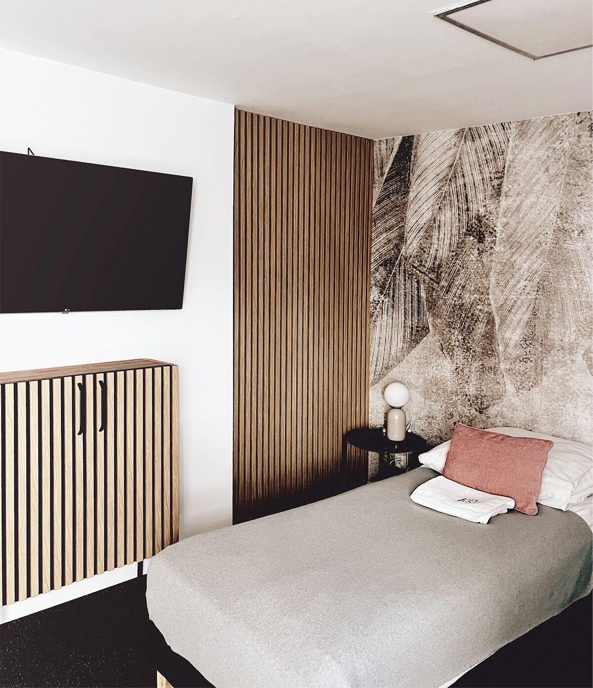 Quarto moderno com cama, mesa de cabeceira, luminária, TV e parede com textura.