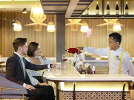 Um restaurante com área de bar, um casal sentado e um garçom servindo uma bebida.
