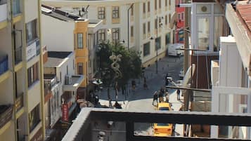 Vista de um ponto alto sobre uma rua da cidade, com edifícios, uma praça central e um corpo de água ao longe.