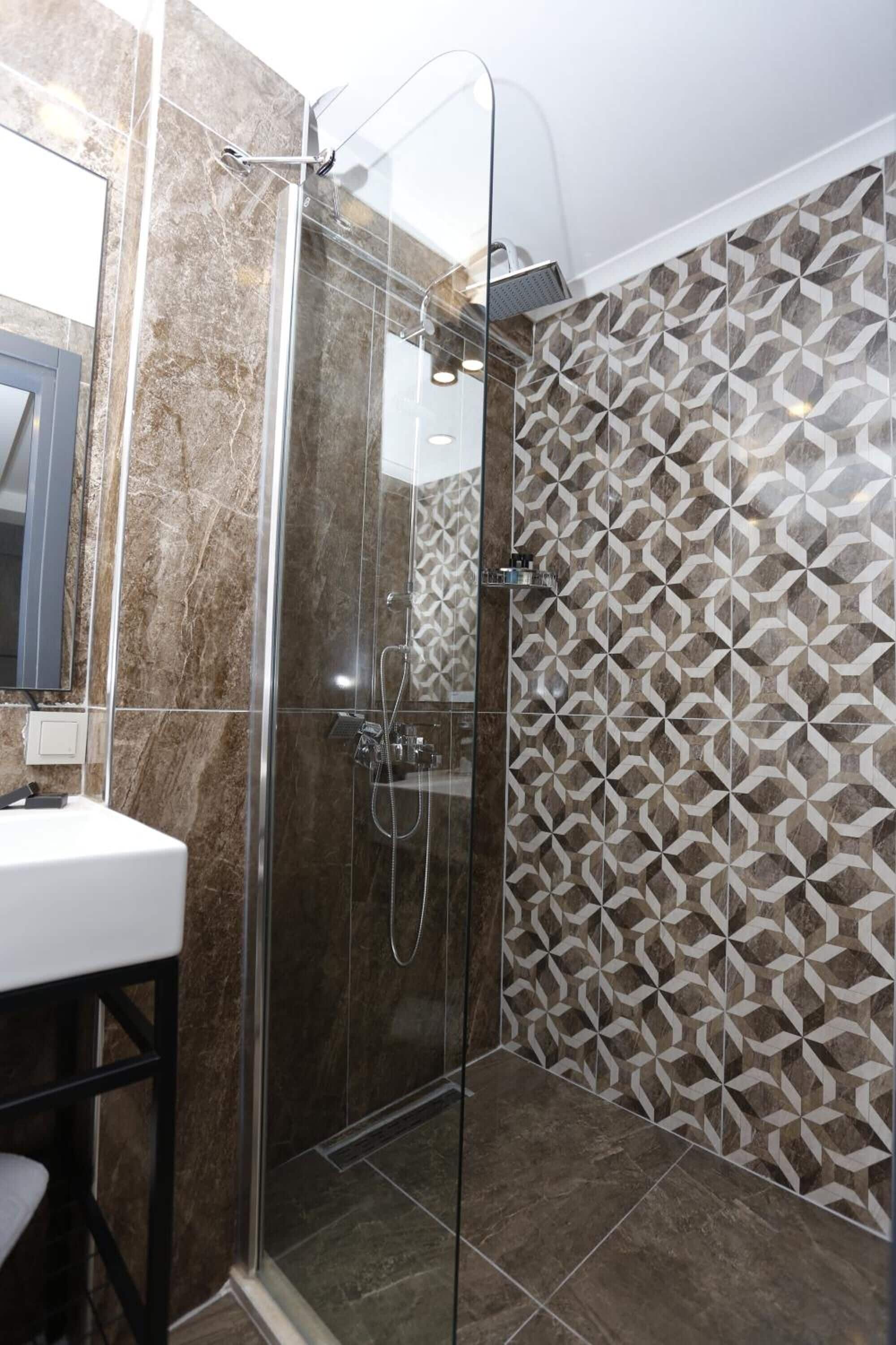 Um banheiro moderno com chuveiro em box de vidro, parede revestida em mármore e painel de azulejos com padrão geométrico.
