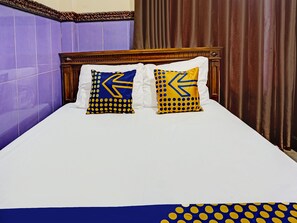 Uma cama com duas almofadas com padrão de flecha azul e amarela, cabeceira de madeira e paredes com azulejos roxos.