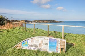 Vista costeira com uma placa de identificação com o título 'PORTHDINLLAEN' e uma cerca de madeira com vista para o mar.