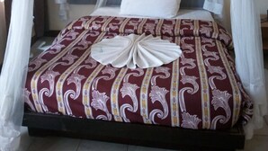 Uma cama com dossel, um edredom estampado e uma arrumação decorativa de almofadas.