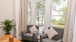 Quarto com duas poltronas cinzentas, uma mesa de centro de madeira e um vaso com planta.