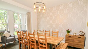 Uma sala de jantar com uma mesa de madeira, cadeiras e um banco. Há também um sofá e um armário com objetos decorativos.