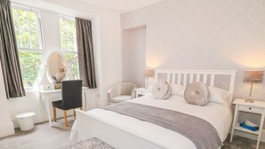 Quarto com cama, escrivaninha, cadeira, mesa de cabeceira e um banquinho.