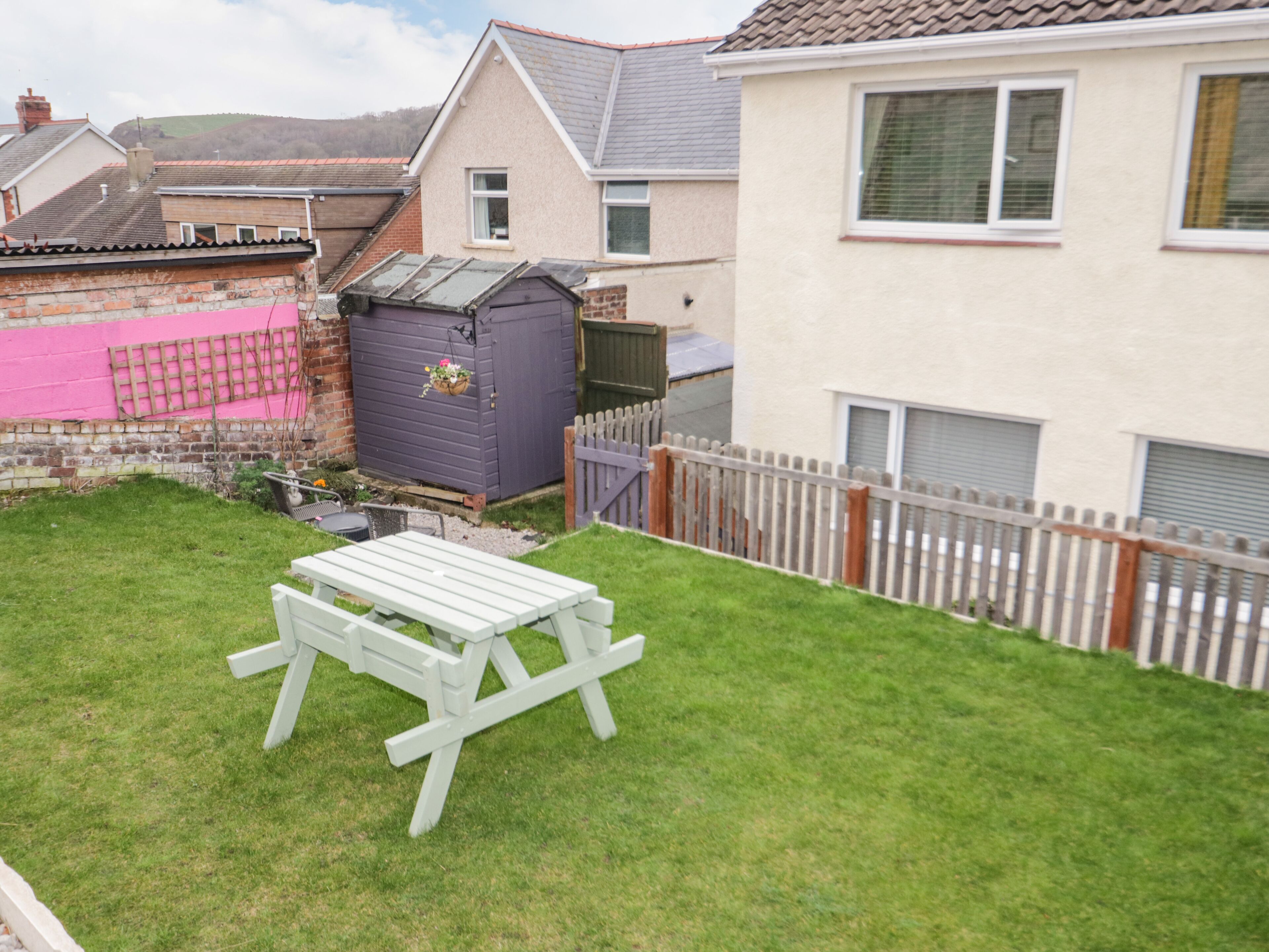 Quintal com mesa de piquenique branca, um galpão e cerca de madeira.