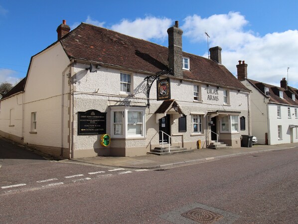 Um edifício branco com uma placa indicando o pub 'The Drax Arms', uma placa anunciando 'Great Home Cooked Food' e uma placa para 'Patrons Car Park'.