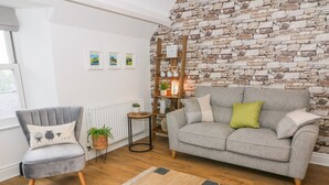 Sala de estar com sofá cinzento, poltrona cinzenta, mesa de centro de madeira, parede de pedra e radiador branco.