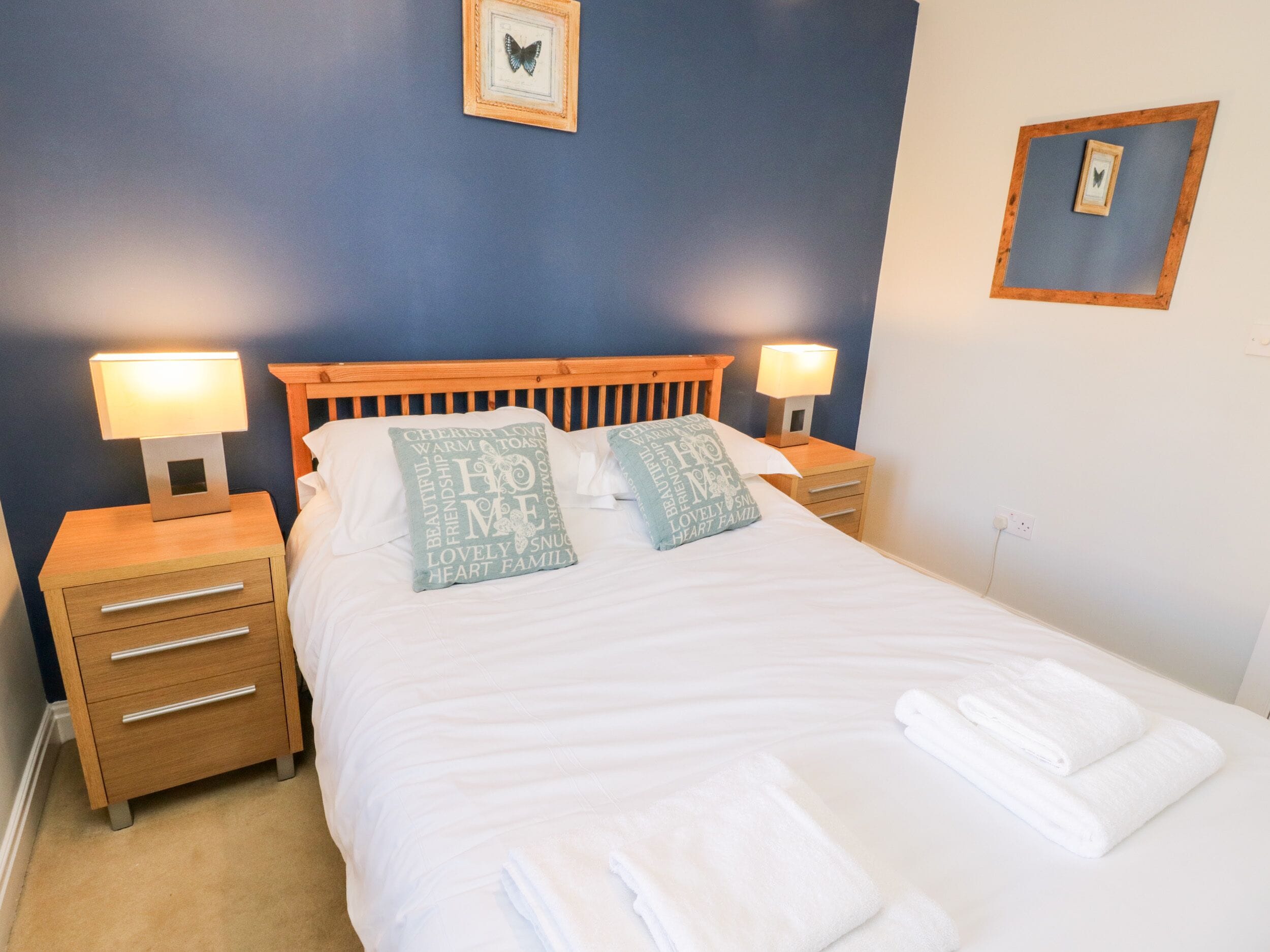 Cama bem arrumada com duas almofadas, cabeceira de madeira e duas mesas de cabeceira com abajures.