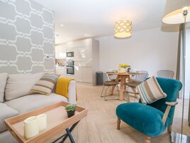 Uma sala moderna com sofá, poltrona verde-água, mesa de centro de madeira e área de jantar com mesa e cadeiras.