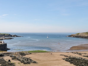 Paisagem costeira com praia arenosa, afloramentos rochosos e mar calmo.