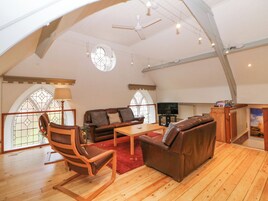 Uma sala de estar ampla em estilo loft, com pé direito alto, piso de madeira, um sofá de couro, uma mesa de centro de madeira e uma televisão.