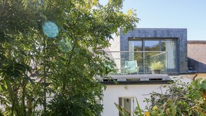 Uma casa moderna com varanda, porta de vidro e vegetação exuberante.