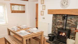 Uma sala de jantar acolhedora com uma mesa de madeira posta para quatro pessoas, uma lareira de tijolos e um relógio na parede.