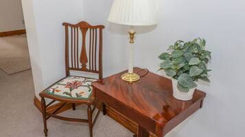 Uma cadeira de madeira com almofada florida, uma luminária de mesa e um vaso com planta.