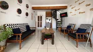 Uma sala de estar com sofá, cadeiras, mesa de centro, televisão e relógios com nomes de cidades.