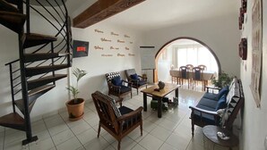 Uma sala de estar ampla com uma escada em espiral, móveis de madeira, um quadro branco e uma vista através de um arco.