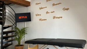 Quarto com sinalização da Netflix, parede com texto decorativo, escada e um banco.