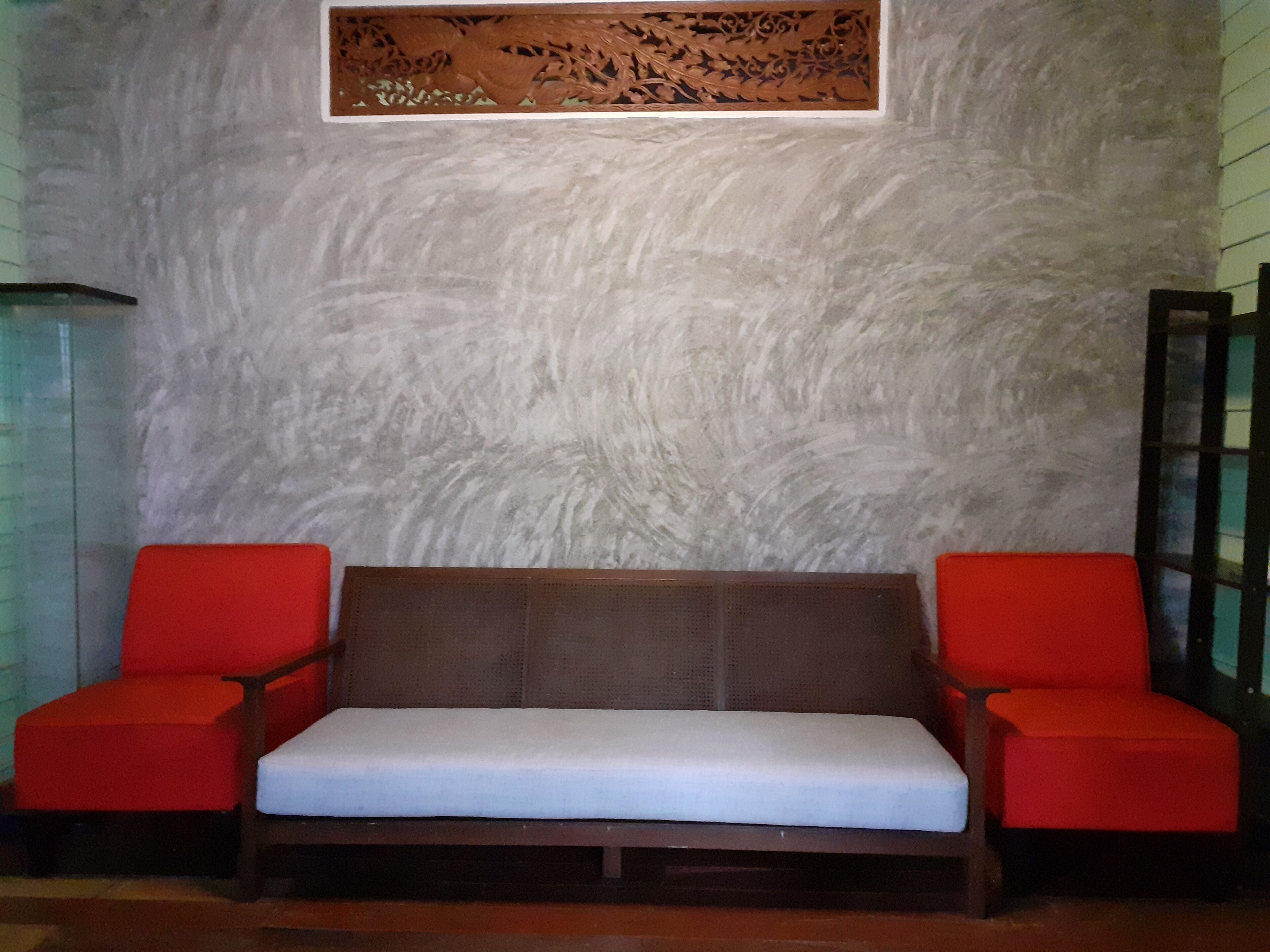 Um quarto com parede texturizada, um banco de madeira com almofada branca e duas cadeiras vermelhas.