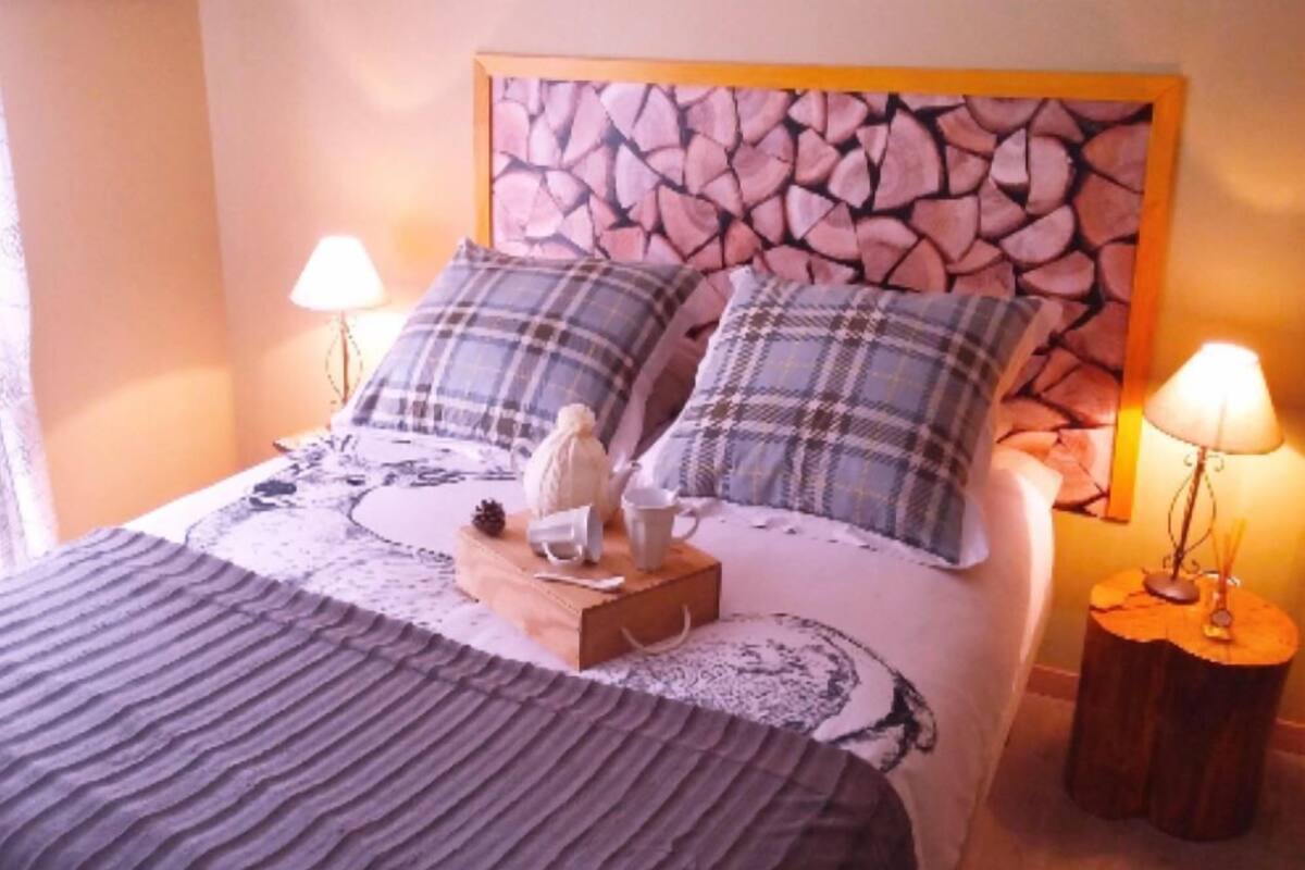 Uma cama bem arrumada com almofadas xadrez, um painel decorativo e duas luminárias de cabeceira.
