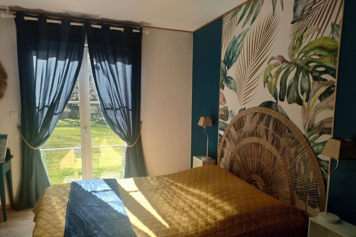 Quarto com cama, janela grande com cortinas, parede com padrão de folha tropical e ventilador.