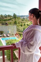 Uma pessoa de roupão ao lado de uma piscina, com vista para vegetação e colinas.
