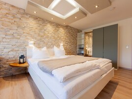 Quarto moderno com parede de pedra, cama com roupa de cama branca, mesa de cabeceira e uma estante embutida.