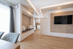 Uma sala de estar moderna com um banco embutido, uma TV de tela plana fixada em uma parede com padrão de tijolos e uma área de jantar com mesa e cadeiras.