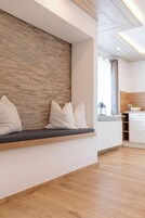 Um interior moderno com um banco embutido, uma área de cozinha e uma janela com cortinas.