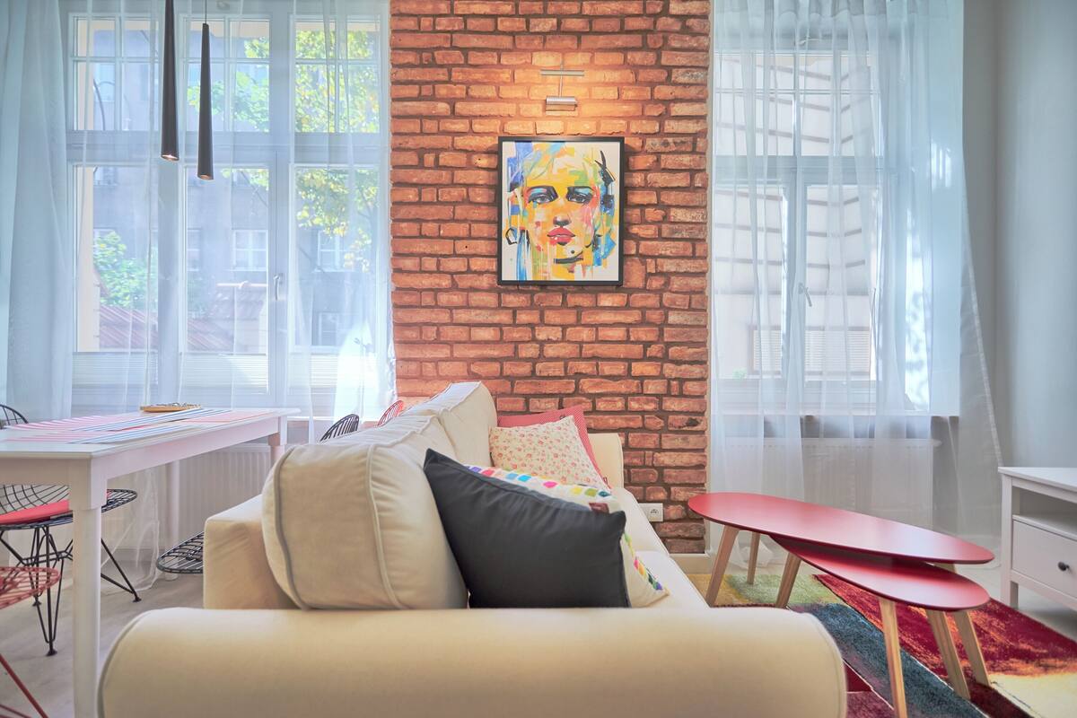 Uma sala de estar moderna com parede de tijolos, um sofá, uma mesinha e um quadro.