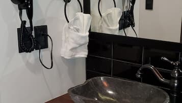 Um banheiro com uma pia grande de pedra, dois secadores de cabelo fixados na parede e uma toalha pendurada em um gancho.