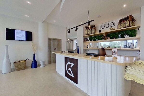 Uma área de recepção moderna com balcão, televisão montada e objetos decorativos em prateleiras.