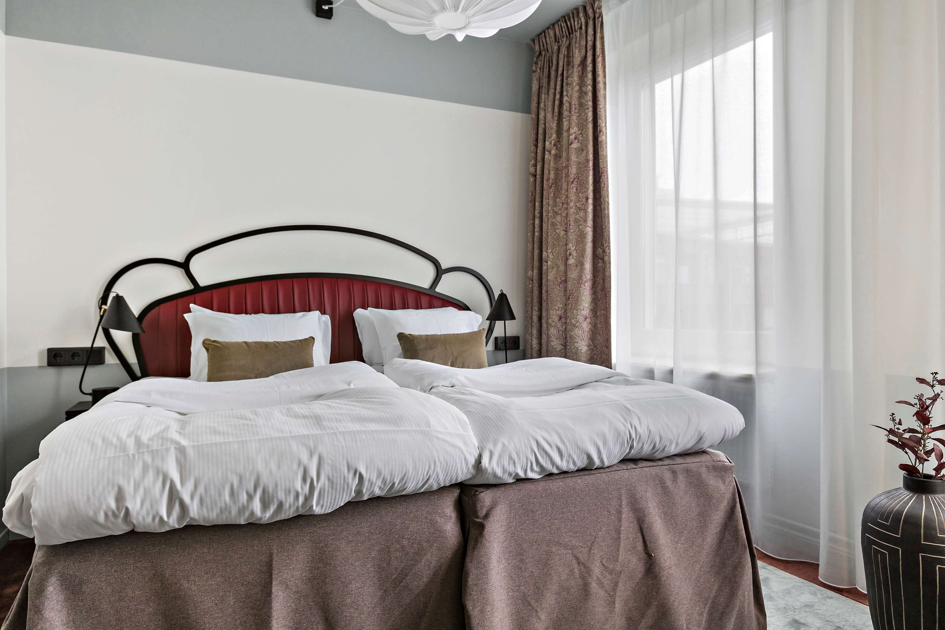 Uma cama bem arrumada com cabeceira vermelha, roupa de cama branca e saia marrom.
