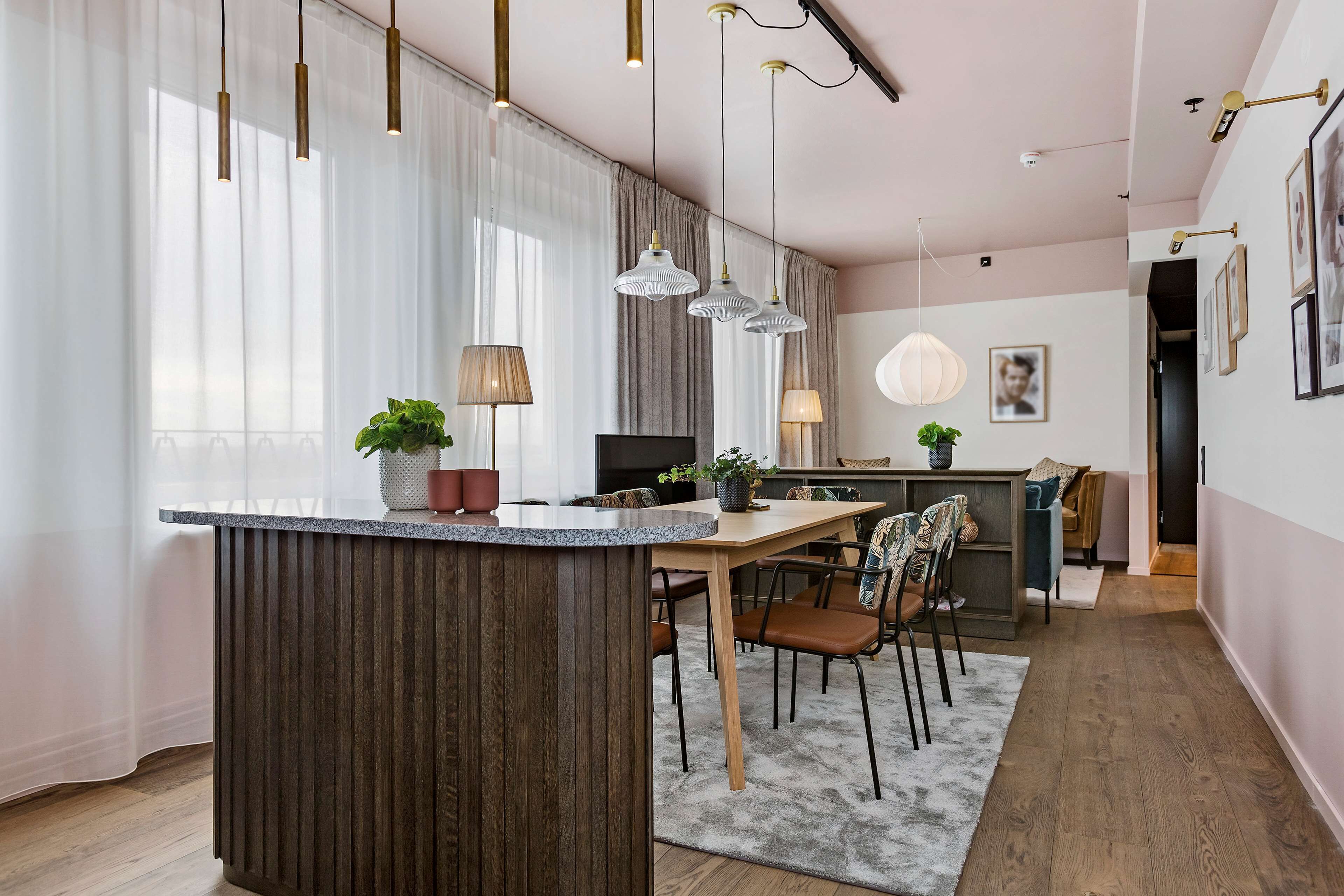 Uma cozinha moderna com ilha central, luminárias pendentes e uma área de jantar com cadeiras e mesa.