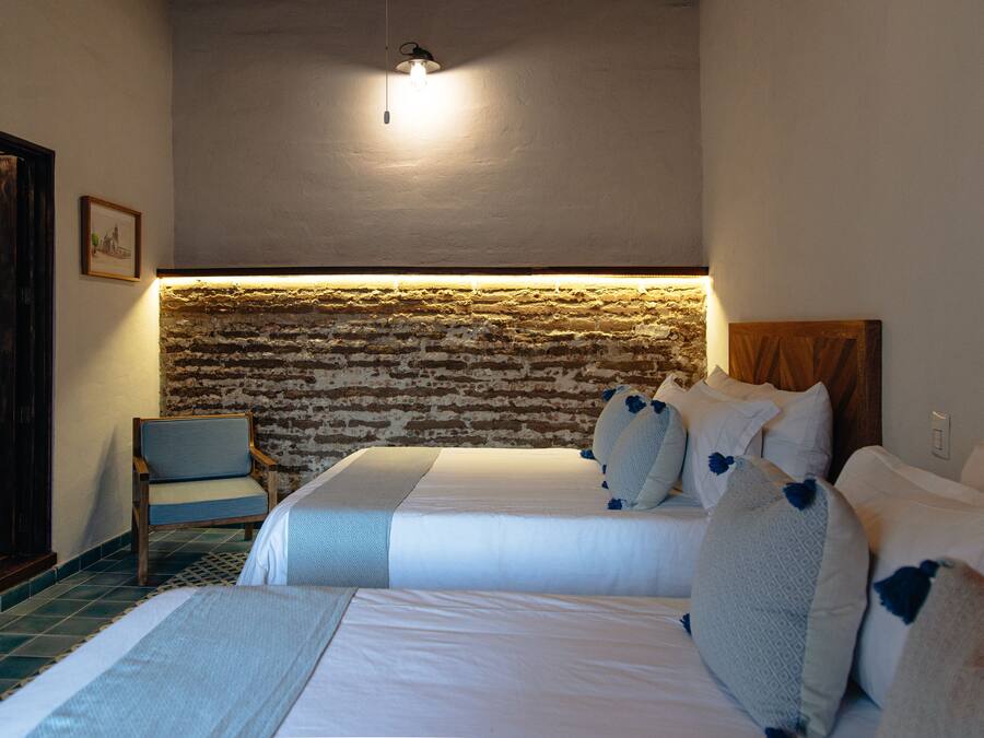 Quarto de hotel com duas camas, uma parede de tijolos, uma porta de madeira e uma cadeira.