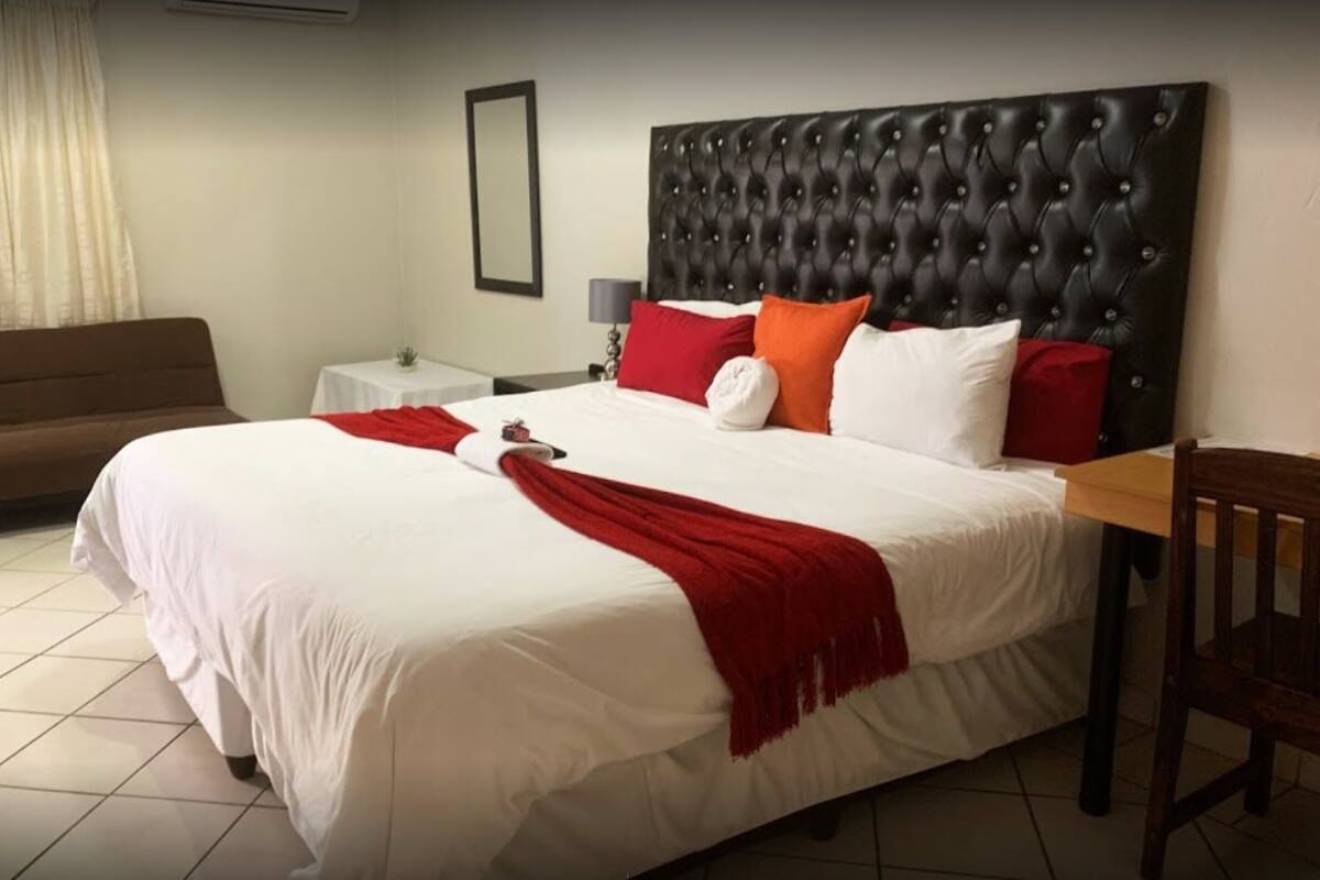 Quarto de hotel com uma cama grande, um sofá castanho, uma mesinha e uma cadeira.