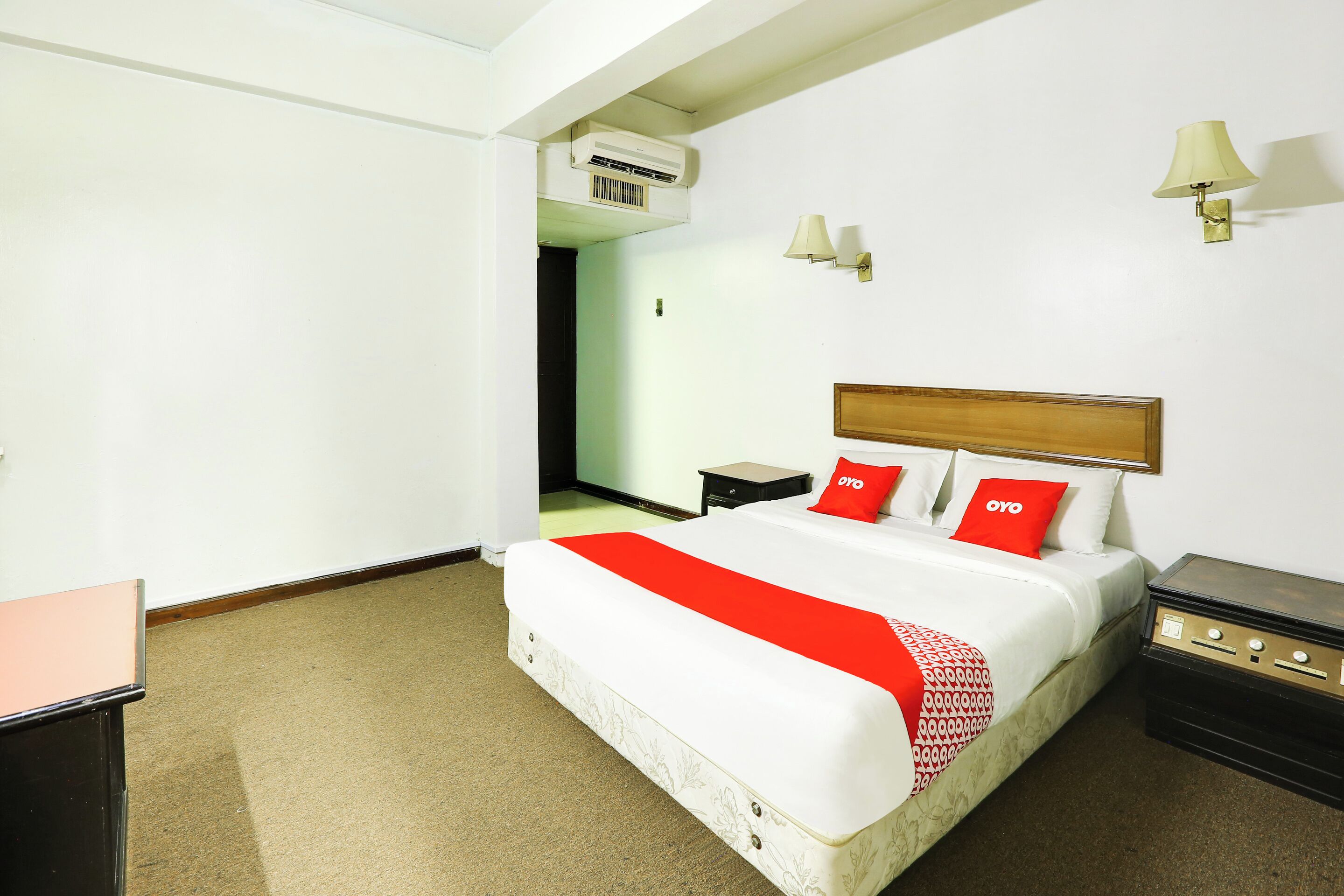 Quarto de hotel com uma cama grande, mesa de cabeceira, ar condicionado e duas luminárias.