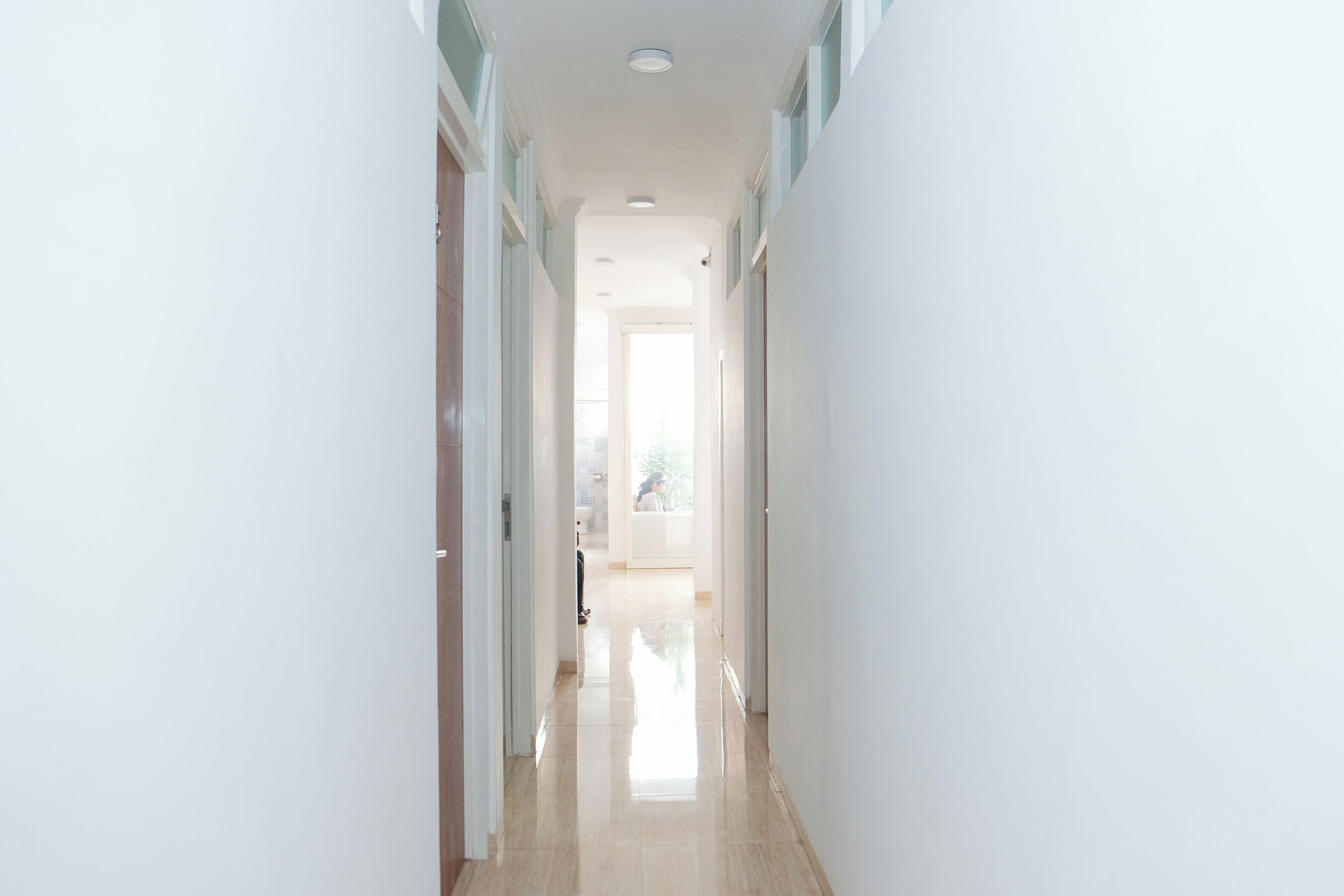 Um corredor claro e bem iluminado com piso brilhante, levando a um quarto com uma grande janela.