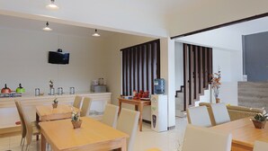 Uma área de refeições moderna com mesas e cadeiras de madeira, uma TV de tela plana na parede e um dispensador de água.